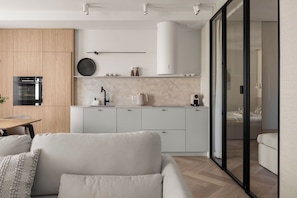 Cozinha moderna com forno embutido, área de refeições com mesa e cadeiras, e sala de estar com sofá.