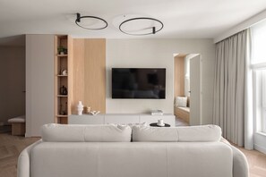 Quarto moderno com uma cama grande, televisão na parede e mesa de cabeceira com abajur.