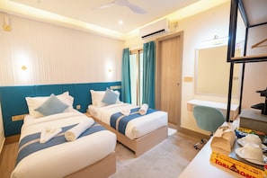Quarto de hotel com duas camas, uma escrivaninha, uma cadeira, um espelho e uma janela com cortinas.