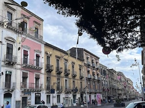 Rua ladeada por edifícios altos, alguns com sacadas, sob um céu nublado.