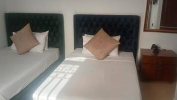 Quarto de hotel com duas camas, cada uma com cabeceira e almofadas. Há uma cômoda de madeira e um espelho na parede.