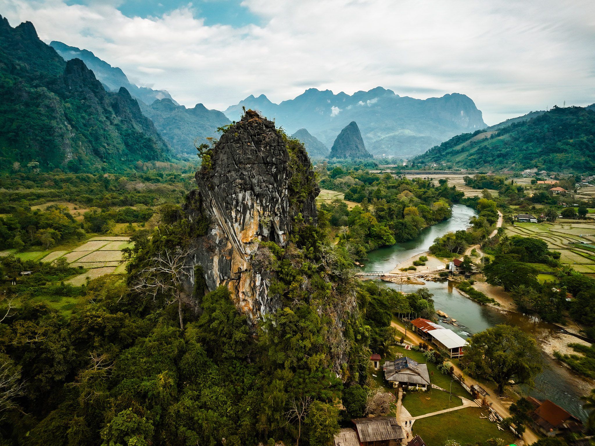 Paisagem montanhosa com uma formação rochosa imponente, um rio e edifícios dispersos.