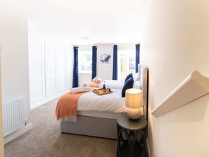Quarto com cama, mesa de cabeceira com abajur, janela com cortinas e radiador.