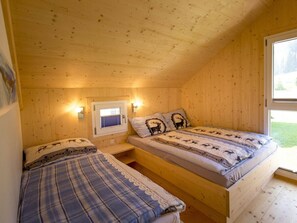 Quarto de cabana com duas camas, janela com persianas e luminárias fixadas na parede.