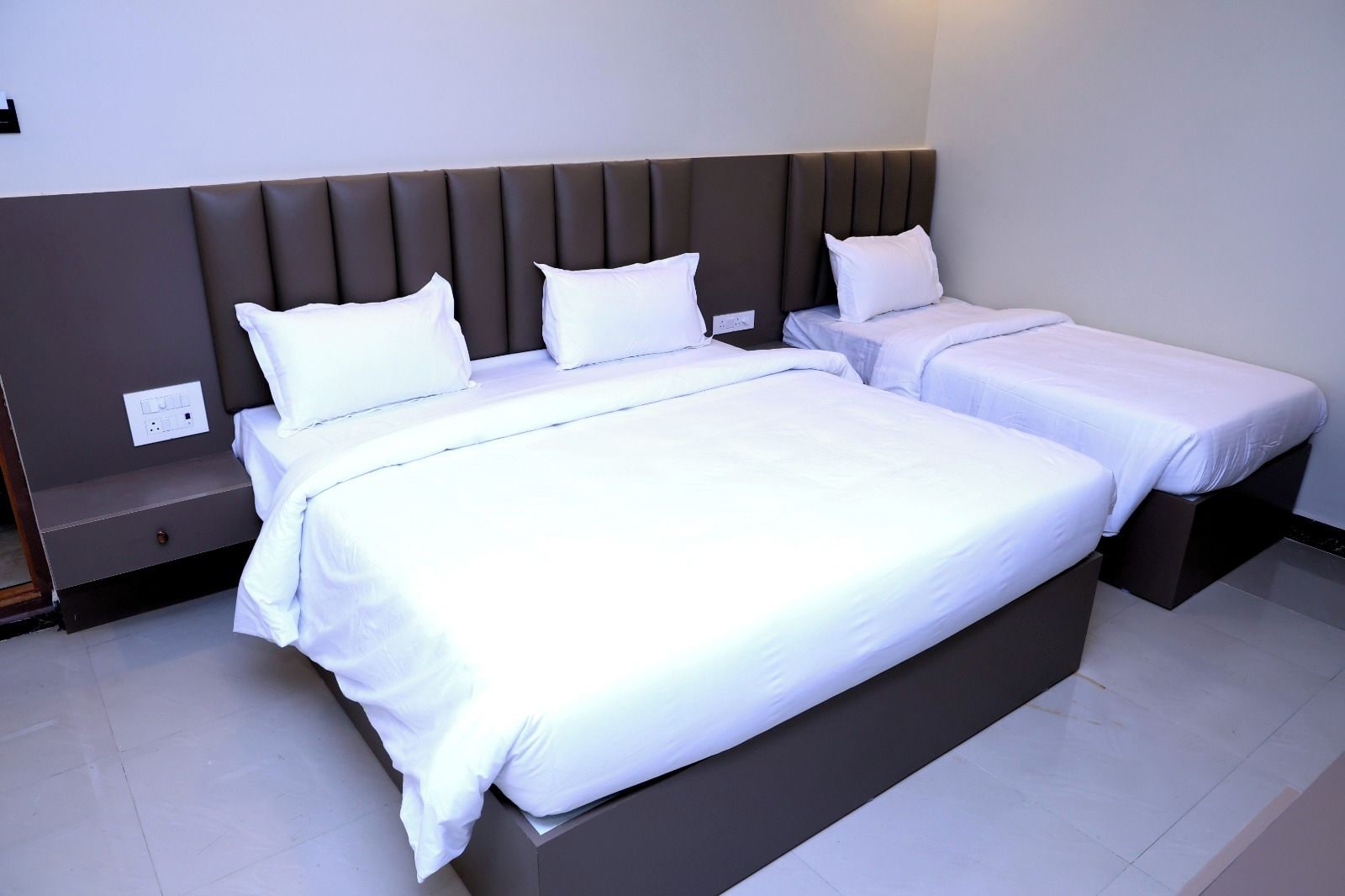 Quarto de hotel moderno com uma cama grande, duas camas menores e um painel de cabeceira acolchoado.
