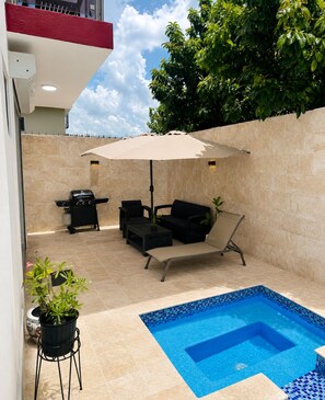 Quintal com piscina, móveis de jardim, churrasqueira e planta em vaso.