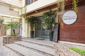 Entrada de restaurante com placa, degraus até a porta e plantas em vasos.