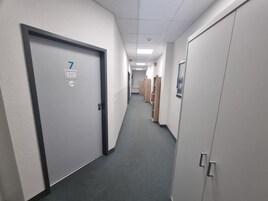 Corredor com porta numerada 7, extintor de incêndio e pôster na parede.
