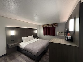 Quarto de hotel moderno com cama grande, mesa de cabeceira, televisão integrada e janela com cortinas.
