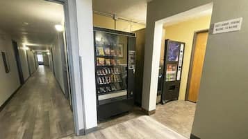 Corredor de hotel com máquinas de venda automática e área de lavanderia para hóspedes.