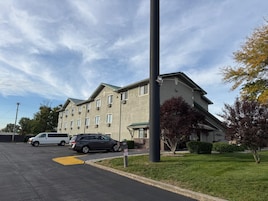 Hotel com vários andares, estacionamento, área gramada e céu claro.