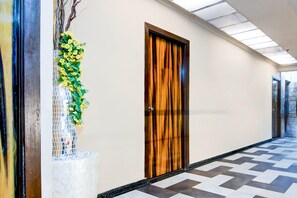 Corredor com piso estampado, porta de madeira e parede decorativa com planta.