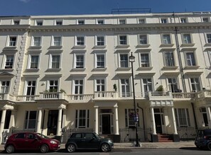 Edifício de vários andares com estilo arquitetônico clássico, com janelas uniformemente espaçadas e fachada simétrica.