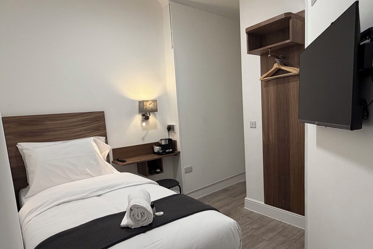 Quarto de hotel com cama, mesa de cabeceira, abajur e televisão na parede.