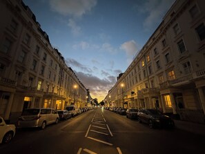 Vista da rua com carros estacionados e edifícios em ambos os lados.