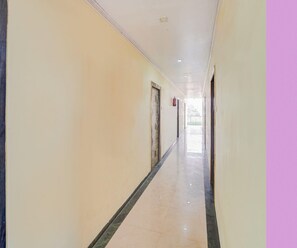 Um corredor comprido e estreito, com portas em ambos os lados, um extintor fixado na parede e piso revestido de azulejos.