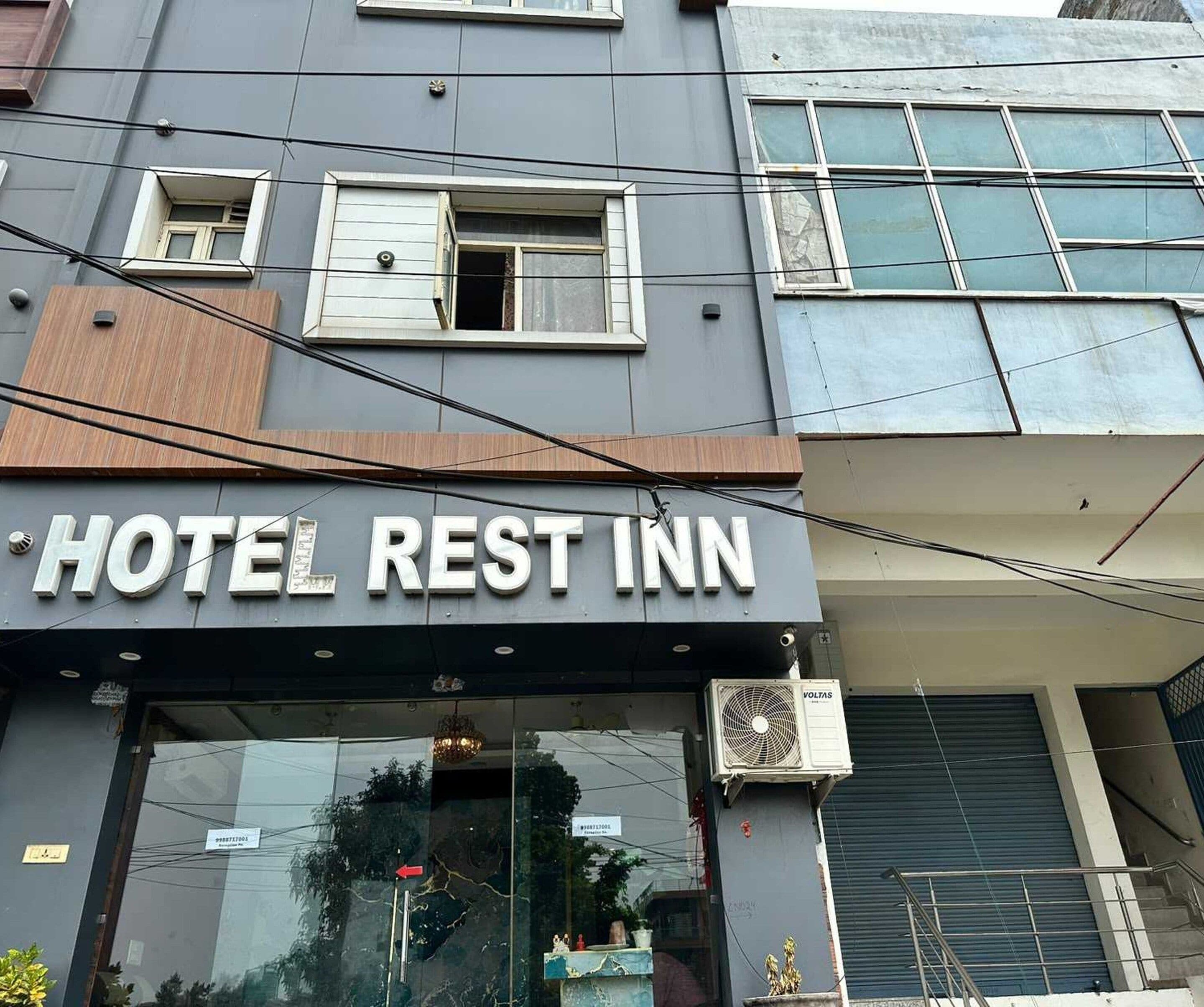 Um hotel chamado 'HOTEL REST INN' com fachada moderna, janelas amplas e unidade de ar condicionado.