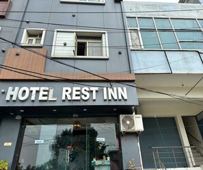 Um hotel chamado 'HOTEL REST INN' com fachada moderna, janelas amplas e unidade de ar condicionado.