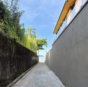 Um caminho de concreto estreito, ladeado por vegetação e um edifício com fachada de madeira.