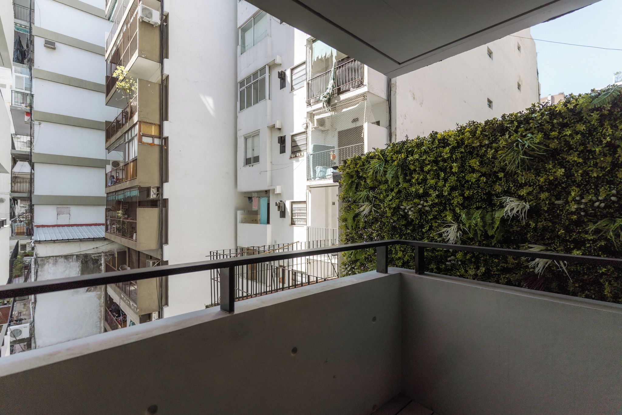 Varanda com grade de metal com vista para área residencial com vários edifícios e sebe verde.
