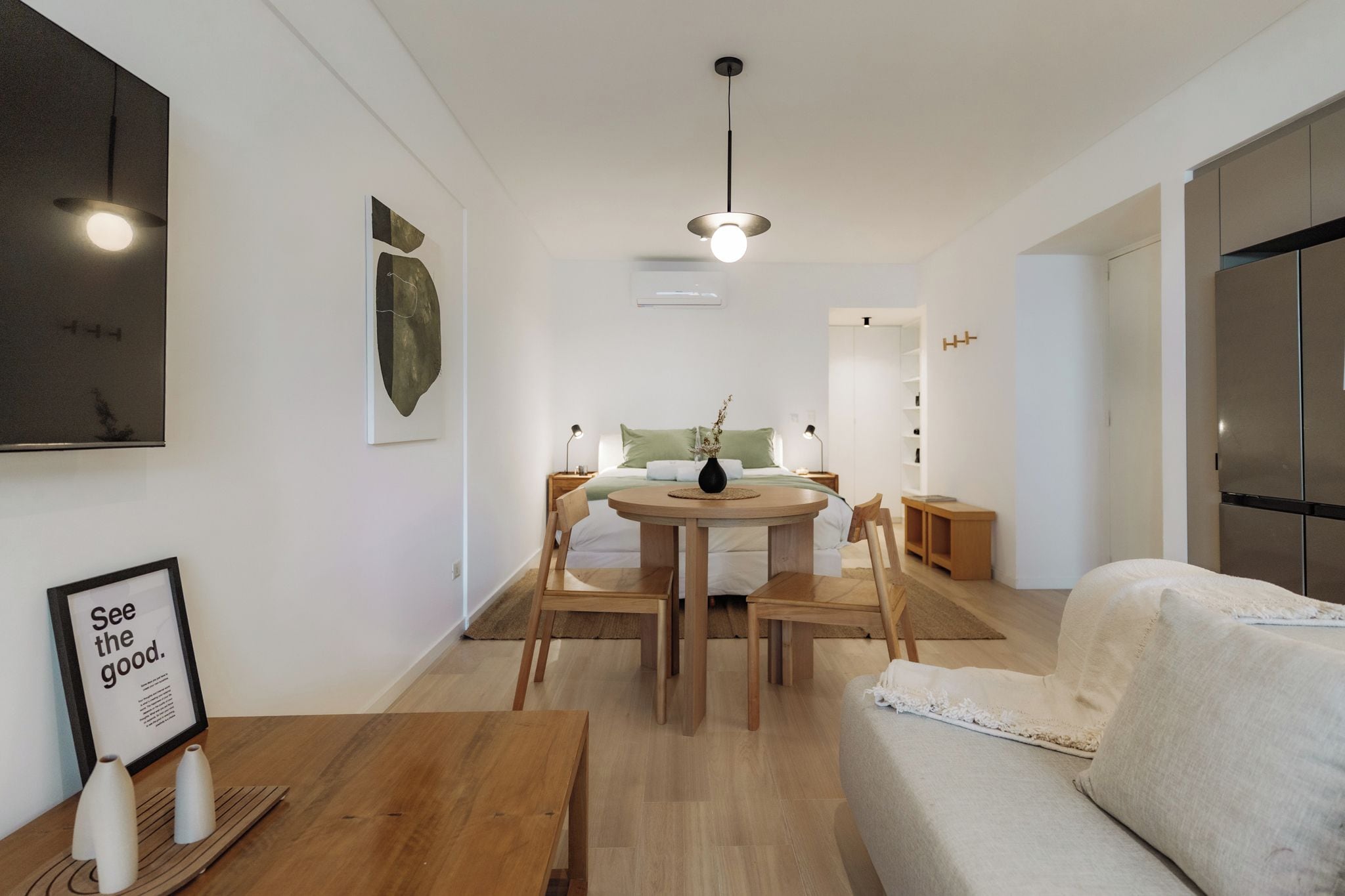 Uma sala de estar moderna com uma mesa redonda de madeira, duas cadeiras, um sofá e um espaço de refeições com toalha de mesa verde.