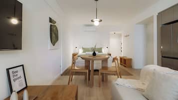 Uma sala de estar moderna com uma mesa redonda de madeira, duas cadeiras, um sofá e um espaço de refeições com toalha de mesa verde.