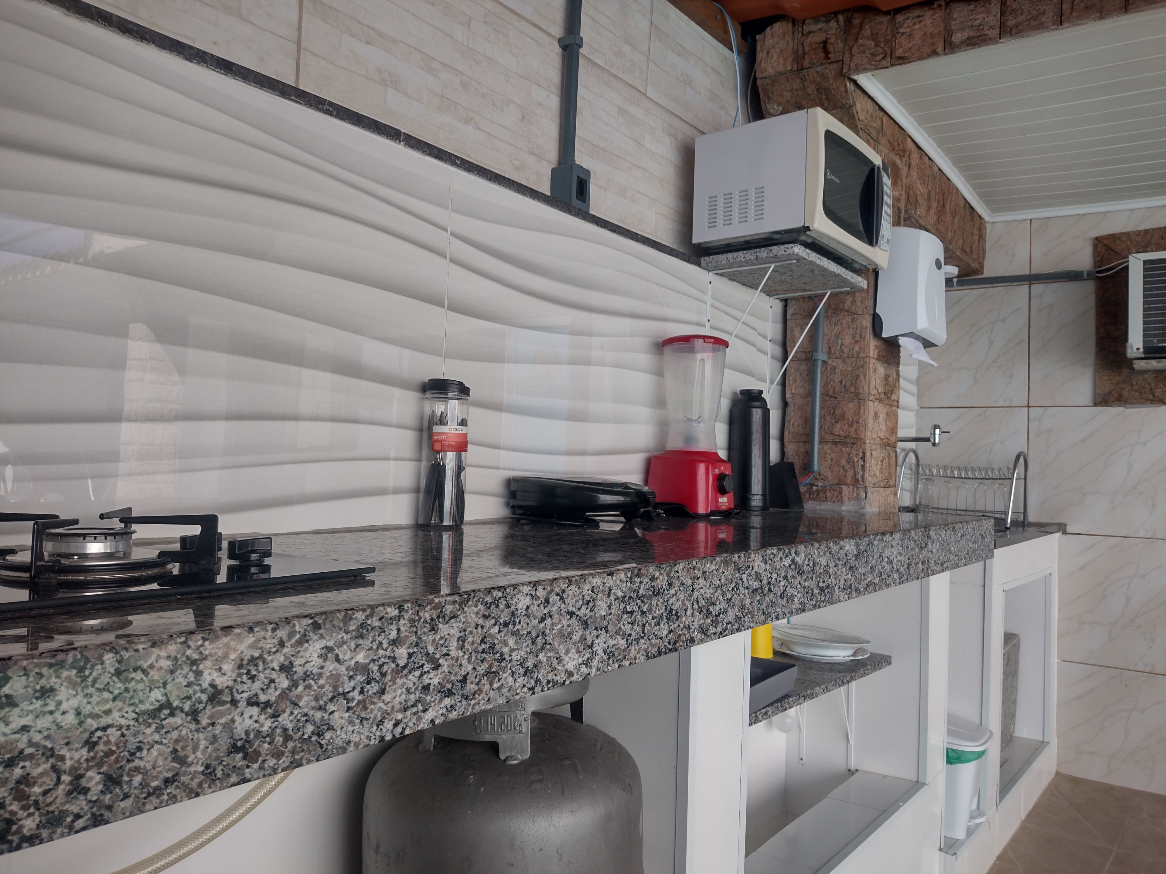 Uma cozinha com bancada de granito, fogão a gás, liquidificador e micro-ondas.