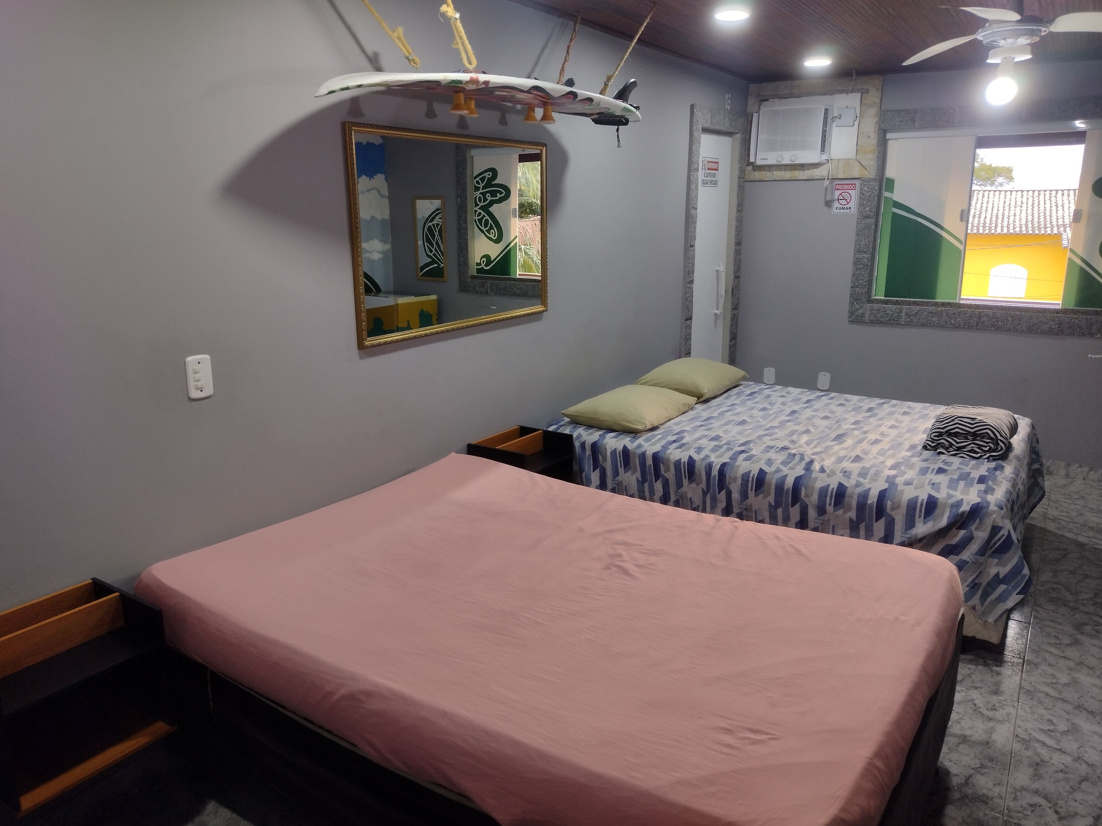 Quarto com uma cama de casal, mesa de cabeceira, espelho e ventoinha no teto.