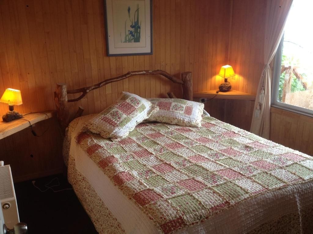 Quarto de madeira com uma cama, duas luminárias de cabeceira e uma janela.