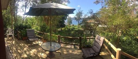 Um terraço ao ar livre com uma mesa redonda, duas cadeiras e um grande guarda-sol.