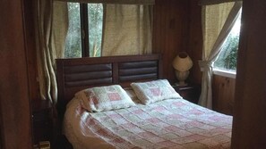 Uma cama com colcha, uma mesa de cabeceira com abajur e cortinas na janela.