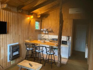 Cozinha compacta com decoração em madeira, área de bar com banquetas, televisão fixada na parede e micro-ondas.