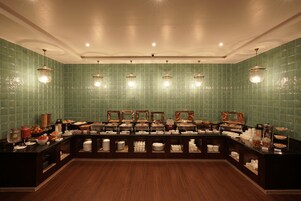 Uma mesa de buffet com várias estações de comida, piso de madeira e paredes com azulejos verdes.