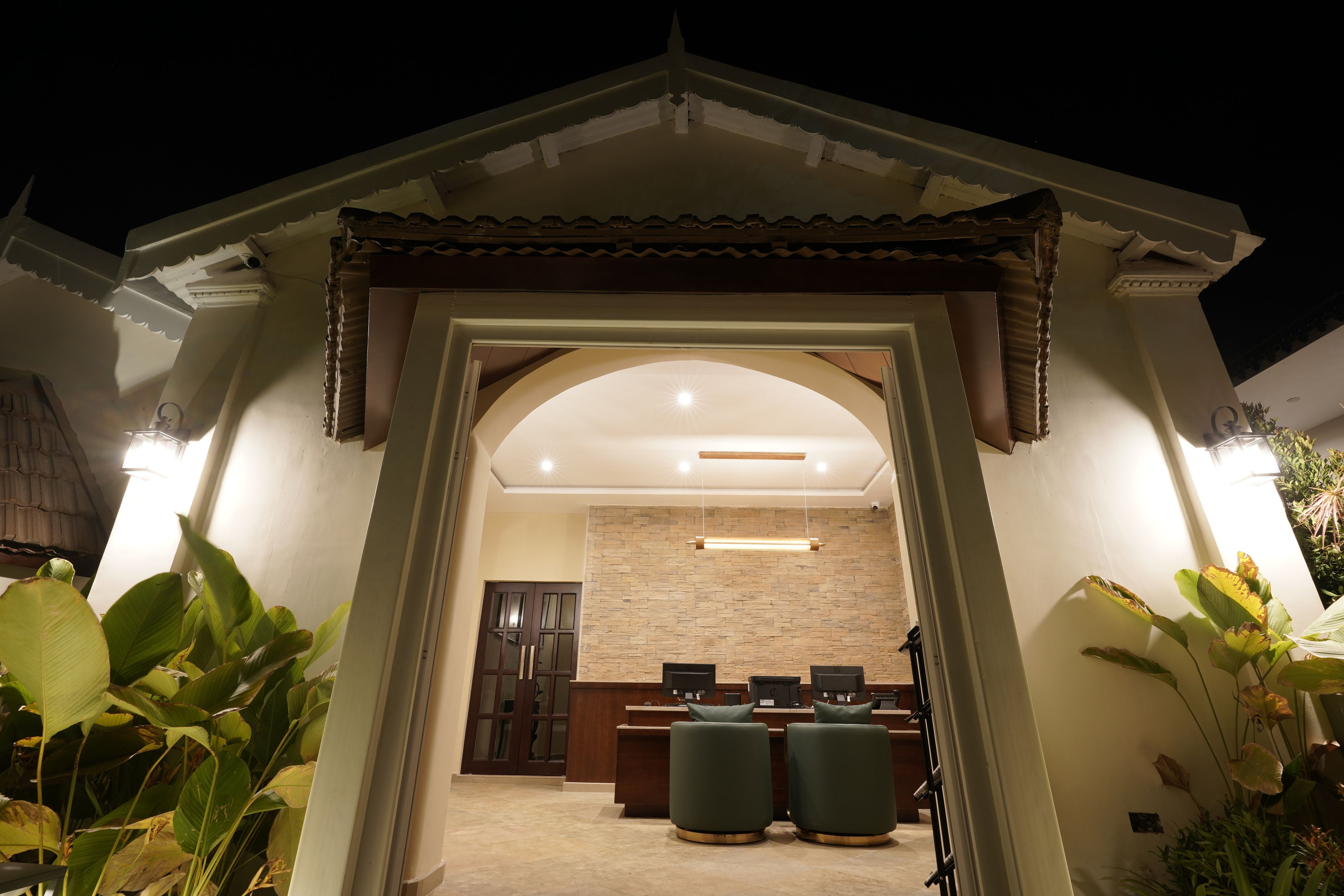 Entrada bem iluminada com telhado cerâmico, parede interior de pedra e área de estar com duas cadeiras.