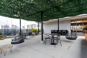 Terraço no telhado com área de estar ao ar livre, vista para a cidade e um edifício moderno ao fundo.