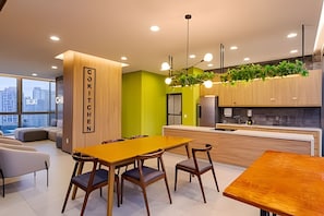 Cozinha moderna com ilha de madeira, área de refeições com mesa amarela e vista para a cidade através de grandes janelas.