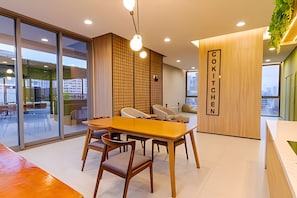 Uma cozinha moderna com bancada de madeira, área de refeições com mesa e cadeiras, e vista através de grandes janelas.