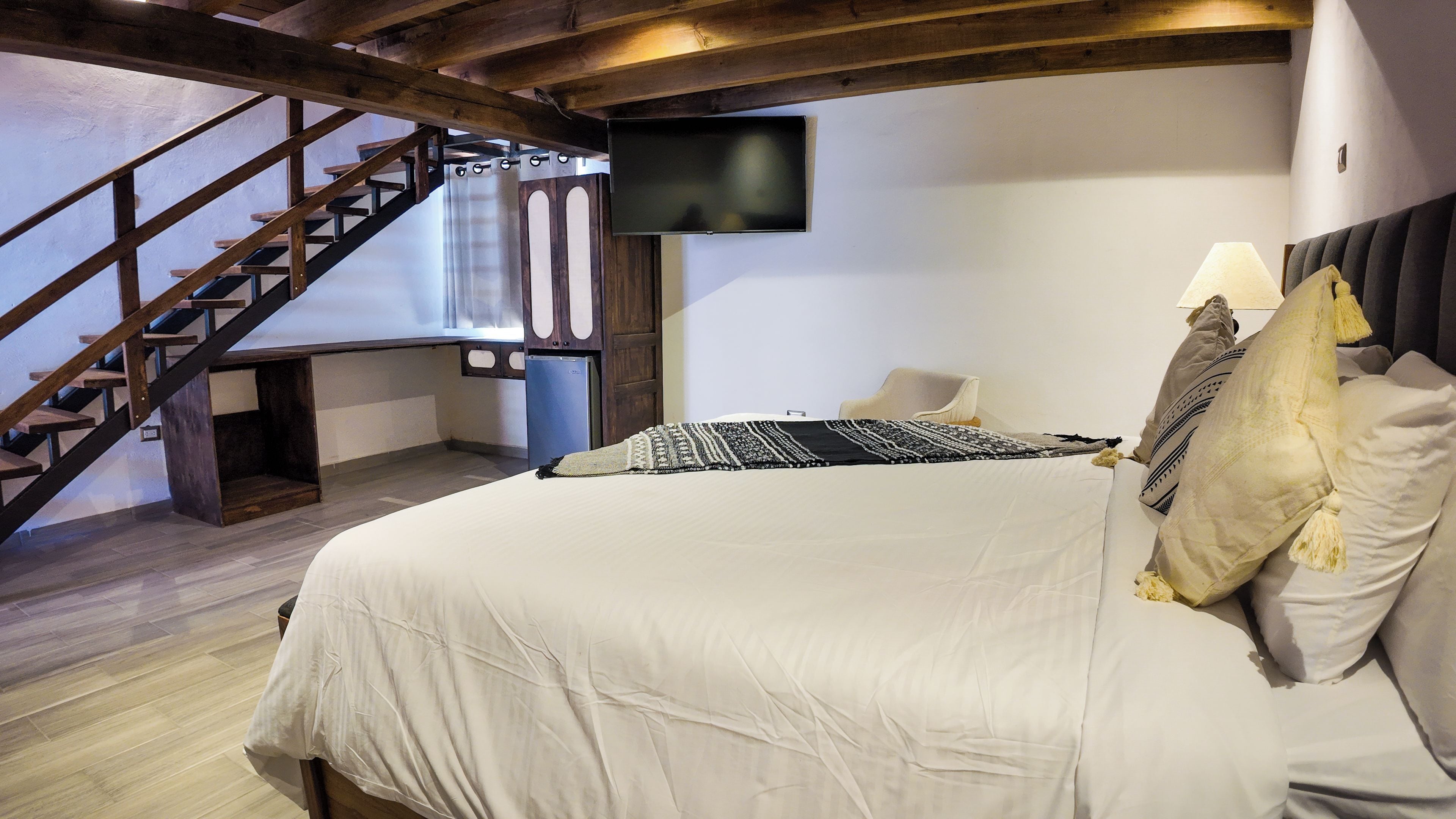 Quarto com cama, televisão fixada na parede e escada.
