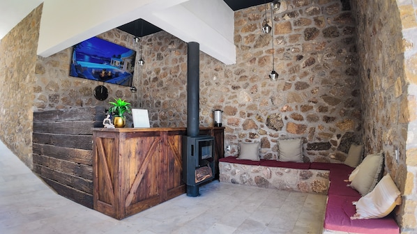 Um quarto com paredes de pedra, um balcão de recepção de madeira, uma lareira e uma televisão na parede.