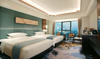 Quarto de hotel com duas camas, uma escrivaninha e uma janela grande com vista.