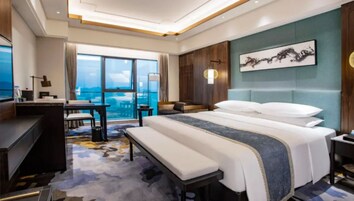 Quarto de hotel moderno com uma cama grande, uma escrivaninha e vista para a cidade.