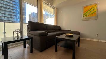 Uma sala de estar moderna com um sofá, duas mesas pretas e vista para a cidade através de grandes janelas.