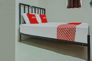 Uma cama com estrutura metálica, roupa de cama branca e almofadas vermelhas.