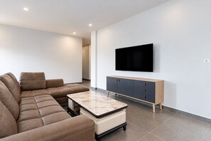 Uma sala de estar moderna com sofá seccional, mesa de centro, TV fixada na parede e armário com gavetas.