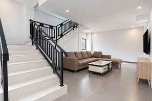 Uma sala de estar moderna com escada, sofá modular, mesa de centro e televisão de tela plana.