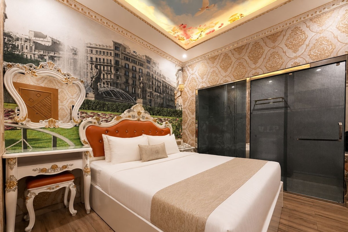 Quarto de hotel com cama, escrivaninha, cadeira, guarda-roupa e um mural na parede.