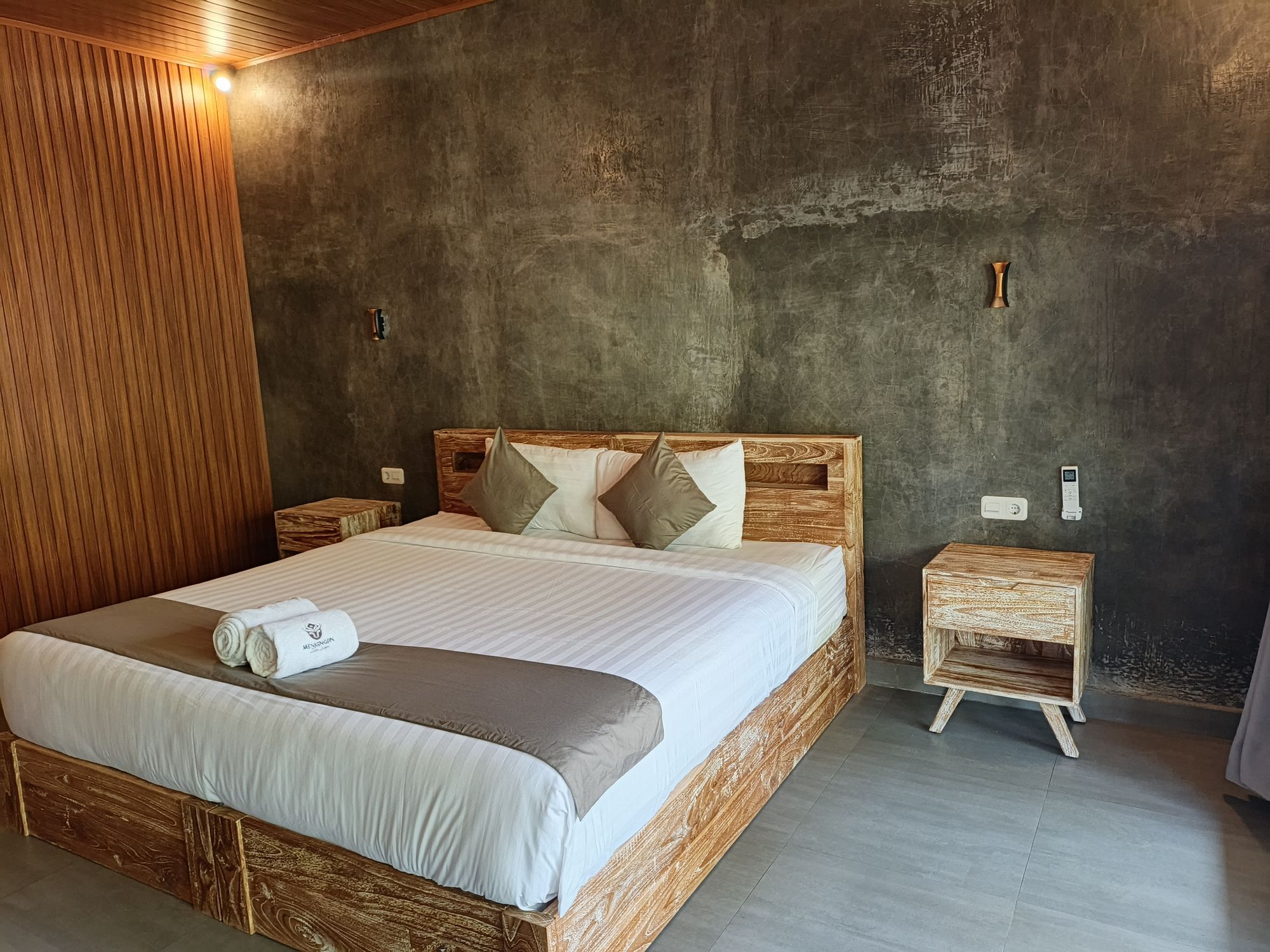 Quarto moderno com cabeceira de madeira, cama grande com roupa de cama branca e mesa de cabeceira com abajur.