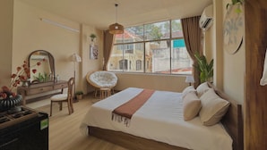 Quarto com cama, poltrona, penteadeira, espelho e janela com vista para prédios.