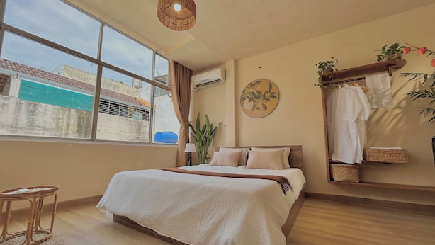 Um quarto com uma janela grande, uma cama, um lustre pendente e uma prateleira na parede com roupas.