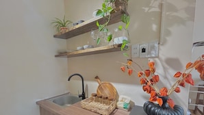 Uma cozinha com armários de madeira, uma pia, uma prateleira de madeira com plantas, um vaso com flores secas e uma cesta trançada.
